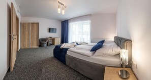 Quarto de hotel com cama, escrivaninha, cadeira, guarda-roupa e televisão.
