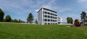 Um edifício de vários andares com telhado plano, cercado por um campo gramado e árvores.