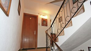 Uma escada com corrimão de madeira e balaústres de metal, conduzindo a uma porta com interruptor de luz acima.