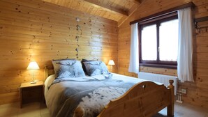 Quarto com painéis de madeira, uma cama, duas luminárias de cabeceira e uma janela com cortinas.