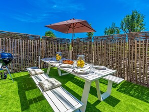 Um pátio externo com mesa posta para refeições, churrasqueira e cerca de madeira.