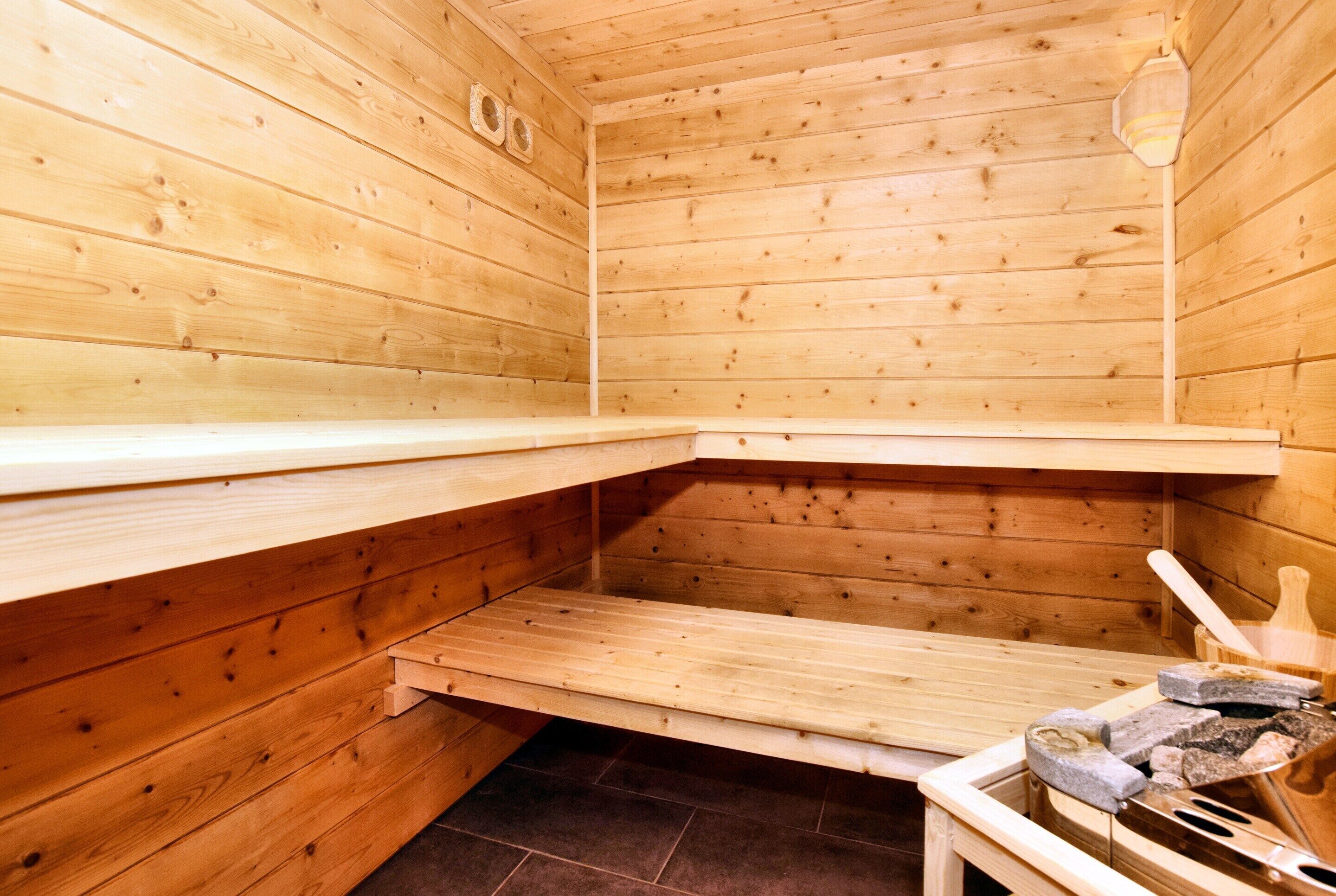 Uma sauna com paredes e bancos de madeira, chão de azulejos e aquecedor de pedra.
