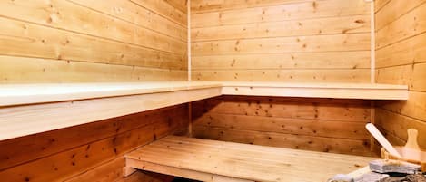 Uma sauna com paredes e bancos de madeira, chão de azulejos e aquecedor de pedra.