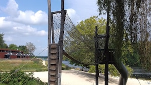 Um parquinho com estrutura de escalada, ponte de corda e área arenosa.