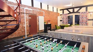 Quarto com mesa de futebol, parede de tijolos, escada em espiral e área de estar com mesa e cadeiras.
