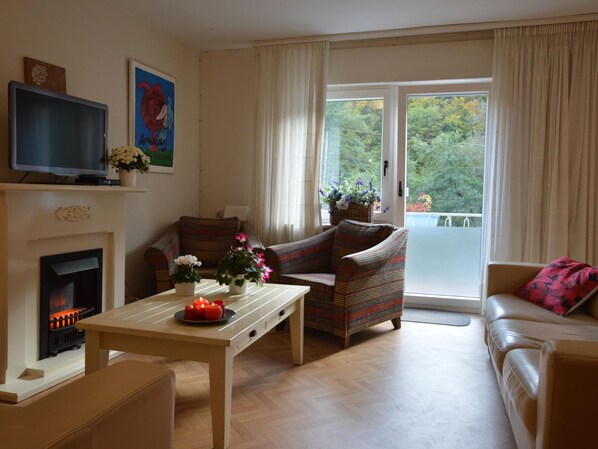 Uma sala de estar com lareira, televisão, sofá, poltrona listrada e uma mesa com flores.