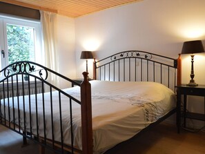 Uma cama de solteiro com cabeceira de madeira e grades de metal, uma mesa de cabeceira com luminárias e uma janela com cortinas.
