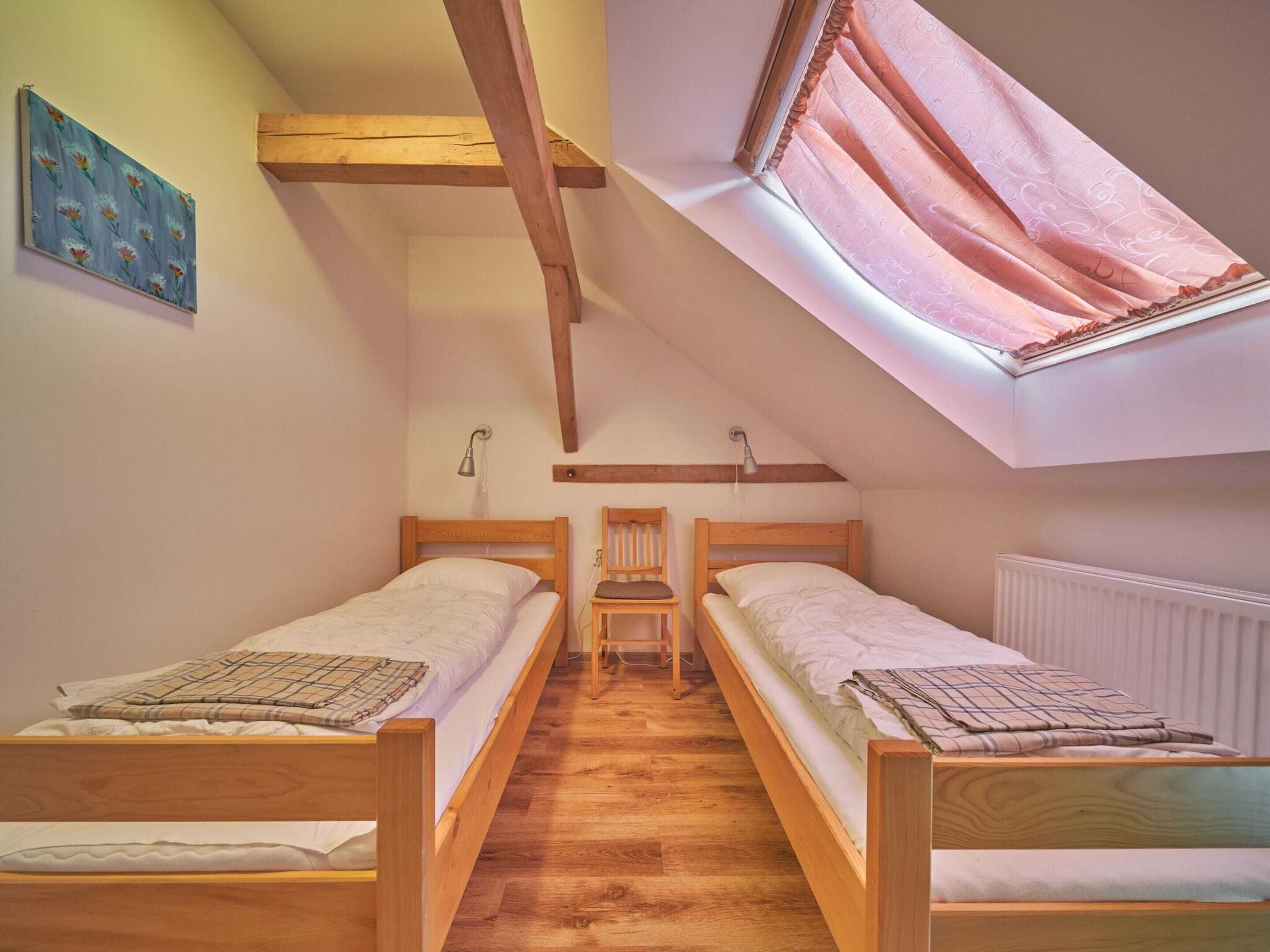 Quarto tipo dormitório com duas camas de madeira, uma mesinha e uma cadeira.