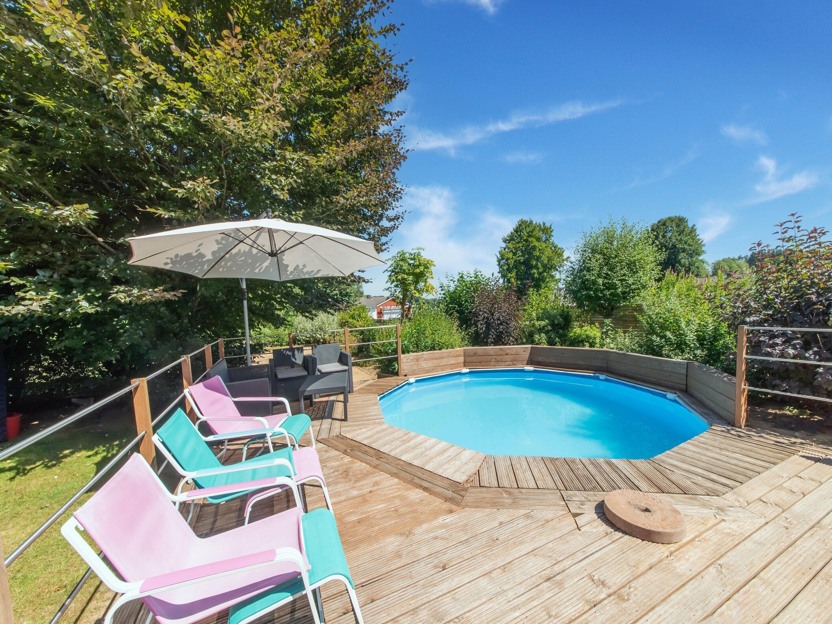 Um quintal com deck de madeira, piscina e cadeiras de sol.