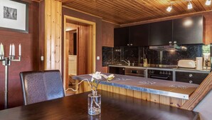 Uma cozinha moderna com armários escuros, teto de madeira e área de jantar com mesa e cadeiras.