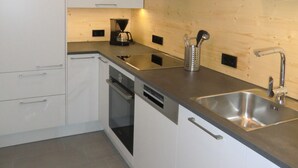 Uma cozinha moderna com armários brancos, uma pia de aço inoxidável e um forno embutido.