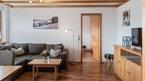 Uma sala de estar aconchegante com um sofá seccional, uma mesa de centro de madeira e uma TV em um móvel de madeira.