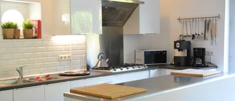 Uma cozinha moderna com armários brancos, fogão a gás, micro-ondas e cafeteira.
