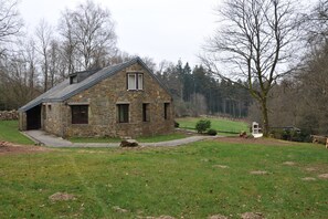 Uma casa de pedra com telhado inclinado, uma pequena varanda e um gramado.