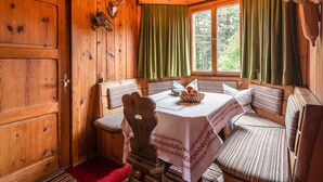 Interior de uma cabana de madeira com uma mesa de jantar, bancos e uma janela com cortinas.