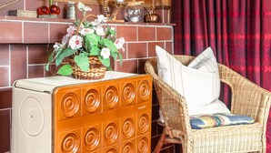 Uma cadeira de vime com almofada, um eletrodoméstico branco e uma cesta de flores em uma parede azulejada.