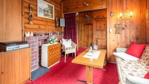 Interior acolhedor de uma cabana de madeira, com área de jantar, sofá, lareira e teto de madeira.