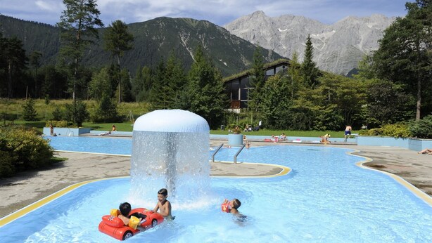 Um parque aquático com um grande tobogã, piscina e montanhas ao fundo.