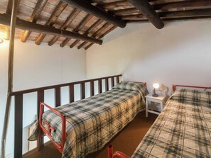 Quarto de dormitório com duas camas individuais, uma pequena mesa de cabeceira com luminária e teto de madeira.
