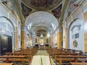 Interior de igreja com bancos de madeira, altar central e um livro aberto grande no chão.