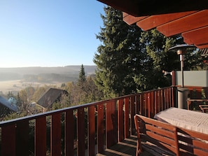 Um deck de madeira com banco e mesa, com vista para um vale arborizado.