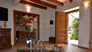 Sala de estar com mesa de centro de vidro, sofá e cozinha visível por uma porta aberta.