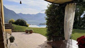 Um pátio com vista para um lago e montanhas, uma mesa de madeira e plantas em vasos.