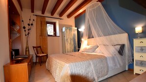 Quarto com cama sob dossel, mesa de cabeceira, cômoda, cadeira e um vaso com elementos decorativos.