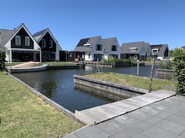 Um canal com um cais para barcos, casas com telhados inclinados e uma área gramada.