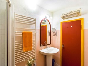 Um banheiro com porta, pia, espelho e porta-toalhas.