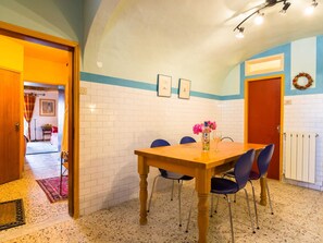 Uma área de refeições com mesa de madeira e cadeiras azuis, paredes revestidas de azulejos brancos e uma paleta de cores azul e branca.