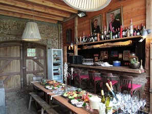 Um bar rústico com paredes de madeira, lareira de tijolos e diversos copos e garrafas nas prateleiras.