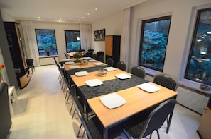 Uma sala de conferências com uma mesa comprida, cadeiras e amplas janelas com vista para árvores.