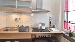 Uma cozinha moderna com exaustor de aço inoxidável, forno embutido, pia e janela com cortina vermelha.