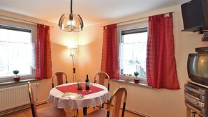 Uma sala de jantar com uma mesa redonda, quatro cadeiras, um candelabro e uma televisão sobre um suporte.