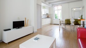 Uma sala de estar moderna com televisão de tela plana, um sofá branco, uma mesa de centro e uma área de jantar com cadeiras e uma mesa.