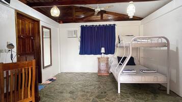 Quarto com cama de solteiro e beliche, uma cadeira de madeira, escrivaninha, espelho e janela com cortinas azuis.