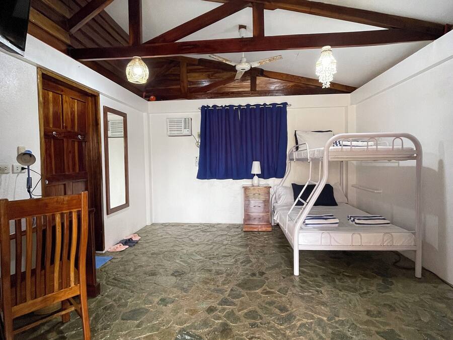 Quarto com cama de solteiro e beliche, uma cadeira de madeira, escrivaninha, espelho e janela com cortinas azuis.
