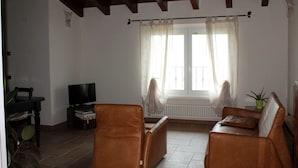 Uma sala de estar com sofá, televisão e janela com cortinas.