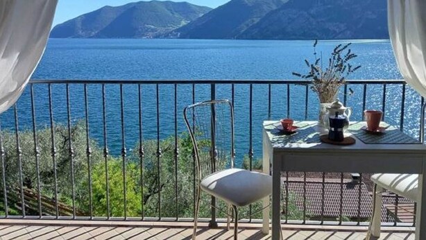 Uma varanda com mesa, cadeiras e vista para o mar e montanhas.