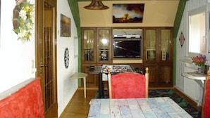Uma área de refeições com mesa de madeira, cadeiras, televisão e mesa de futebol.