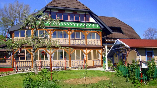 Uma casa tradicional de dois andares com varanda, rodeada por um jardim bem cuidado.