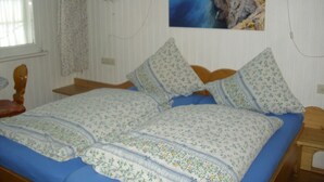 Quarto com cama, almofadas, cabeceira de madeira, mesa de cabeceira e um quadro na parede.