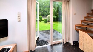 Quarto com porta de correr de vidro que dá para um jardim, escada de madeira e uma televisão sobre suporte de madeira.