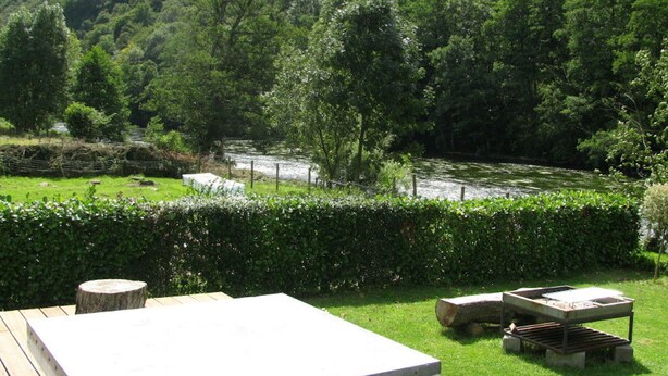Um jardim à beira-rio com um deck de madeira, um banco de pedra e uma mesa branca.