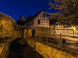 Um edifício histórico com uma ponte de pedra e um espaço pavimentado com bancos.