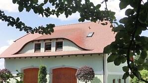 Uma casa de dois andares com telhado de telhas vermelhas, um pequeno claraboia e porta de garagem de madeira.