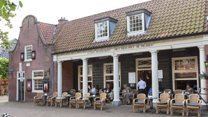 Um café com mesas ao ar livre e uma placa com a inscrição 'Het Huis Met De Pilaren'.