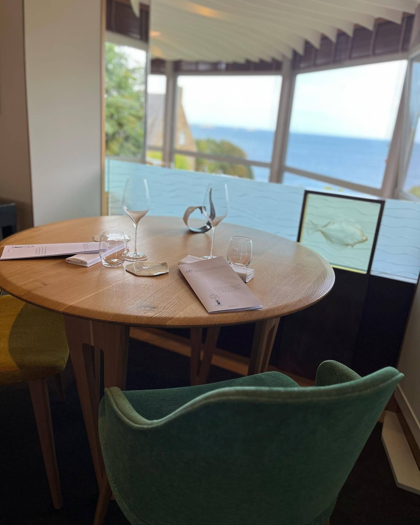 Uma mesa posta para dois, com menu, um cartão de menu, um copo de água e um copo de vinho.