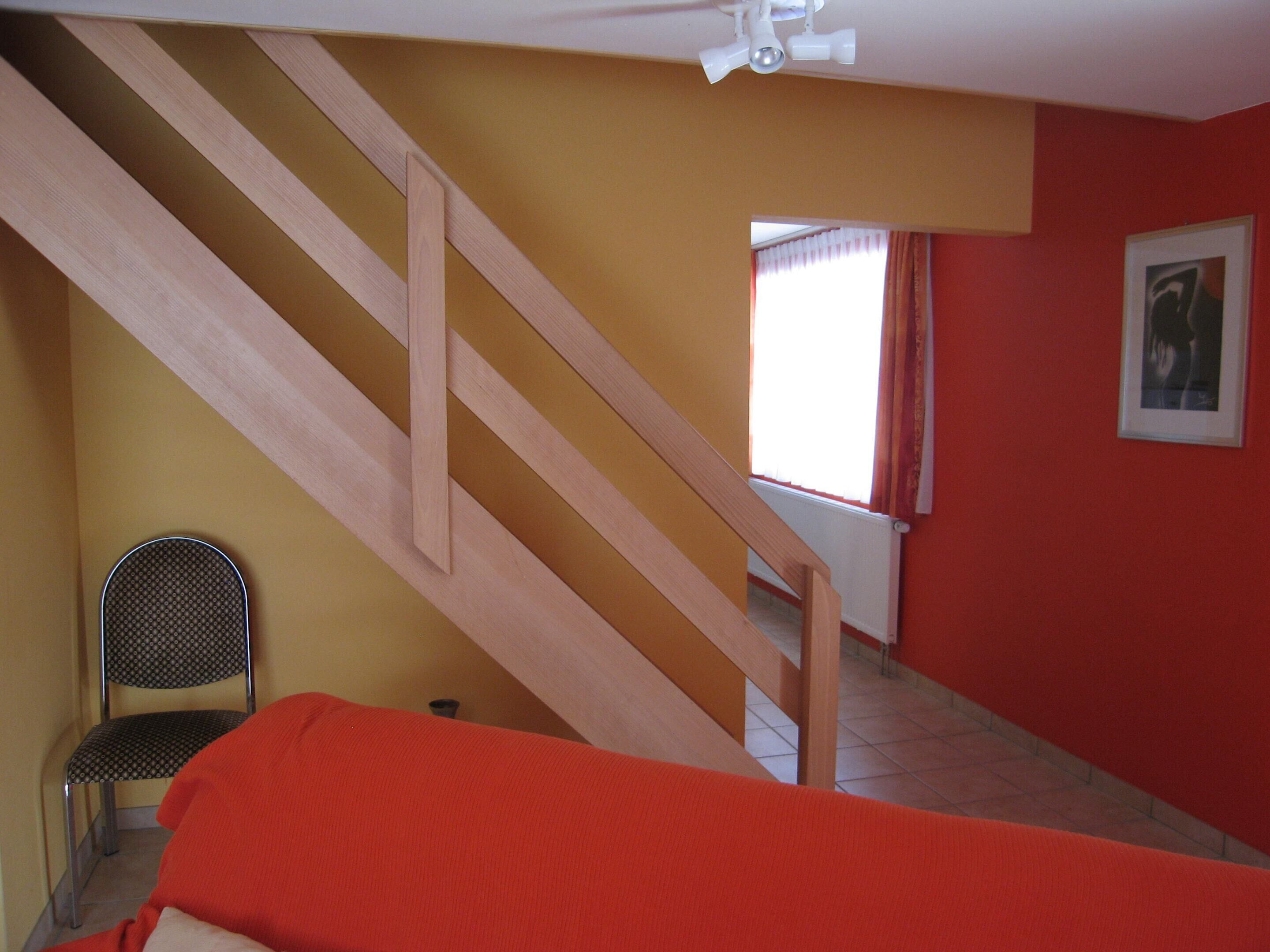 Quarto com escada de madeira, uma cadeira e uma cama.